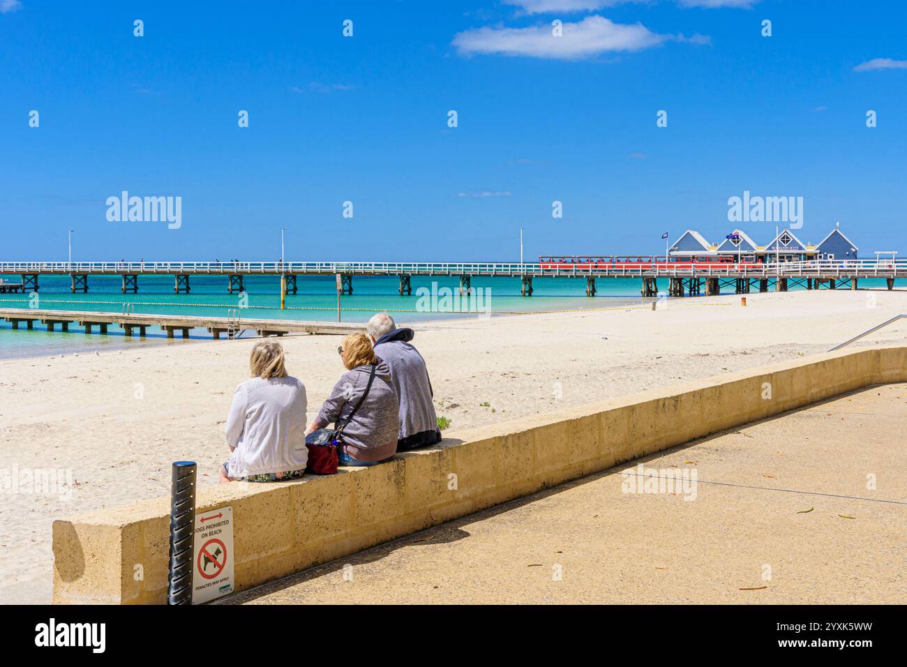 People seated on a wall overlooking Busselton Jetty and the beach ...
