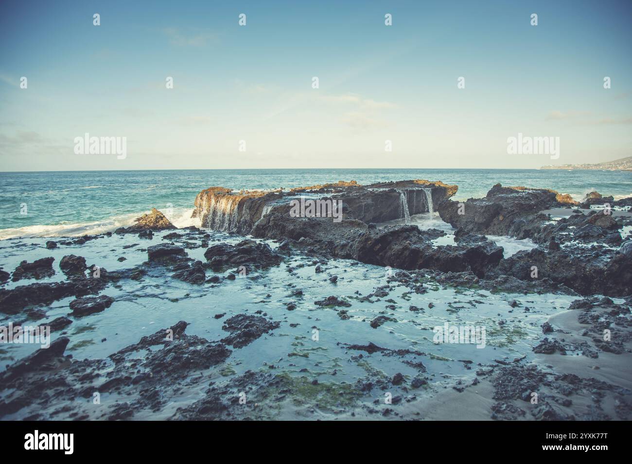 A view of a rocky beach landscape featuring wave waterfalls and a large ...