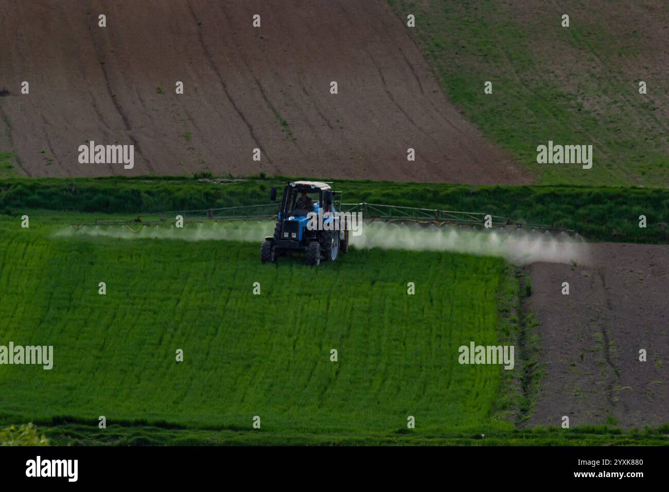 Aerial view of tractor spraying crop in green farm fields with ...