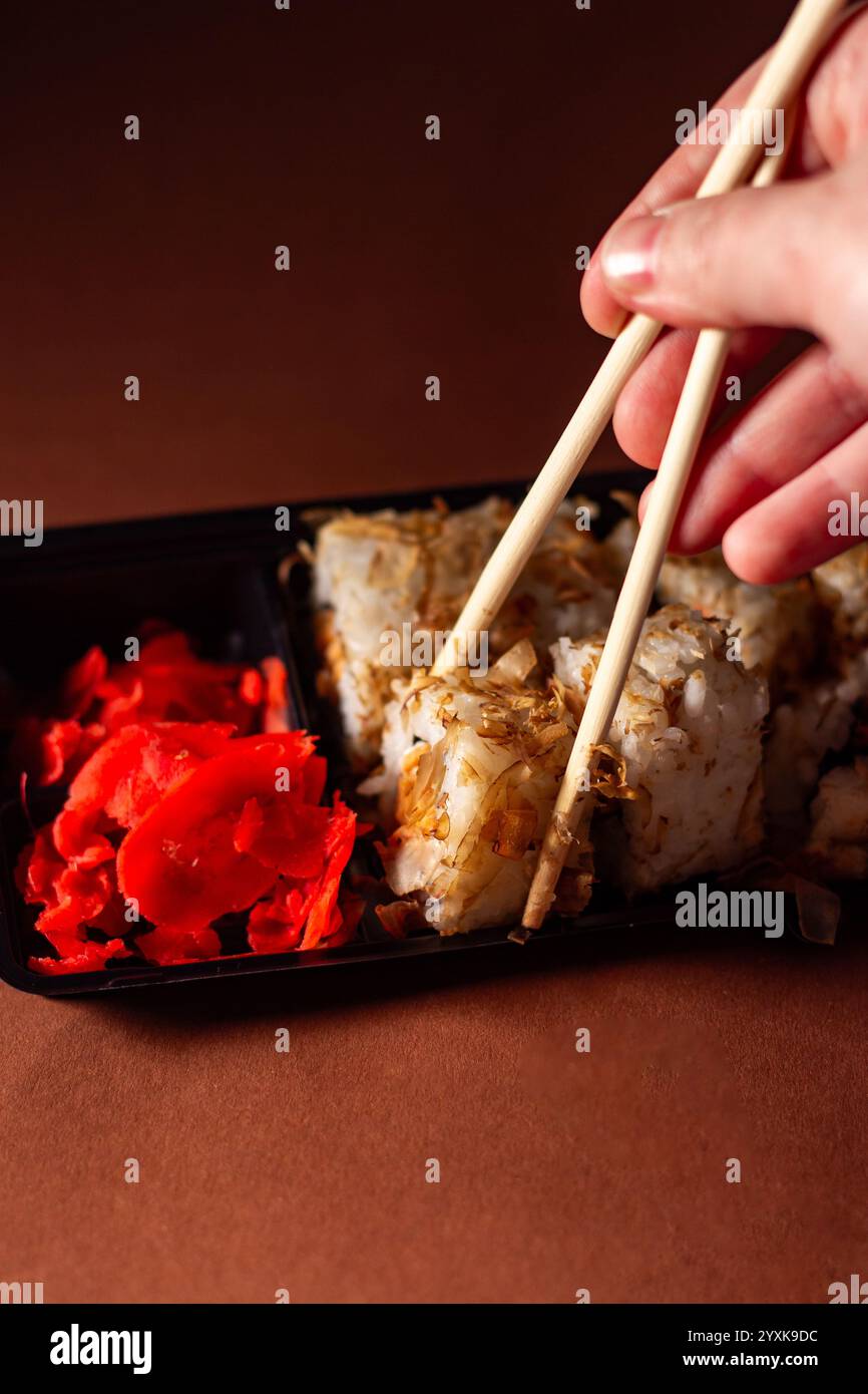 Hand with chopsticks taking portion of sushi roll. Sushi rolls with salmon cream cheese and ...