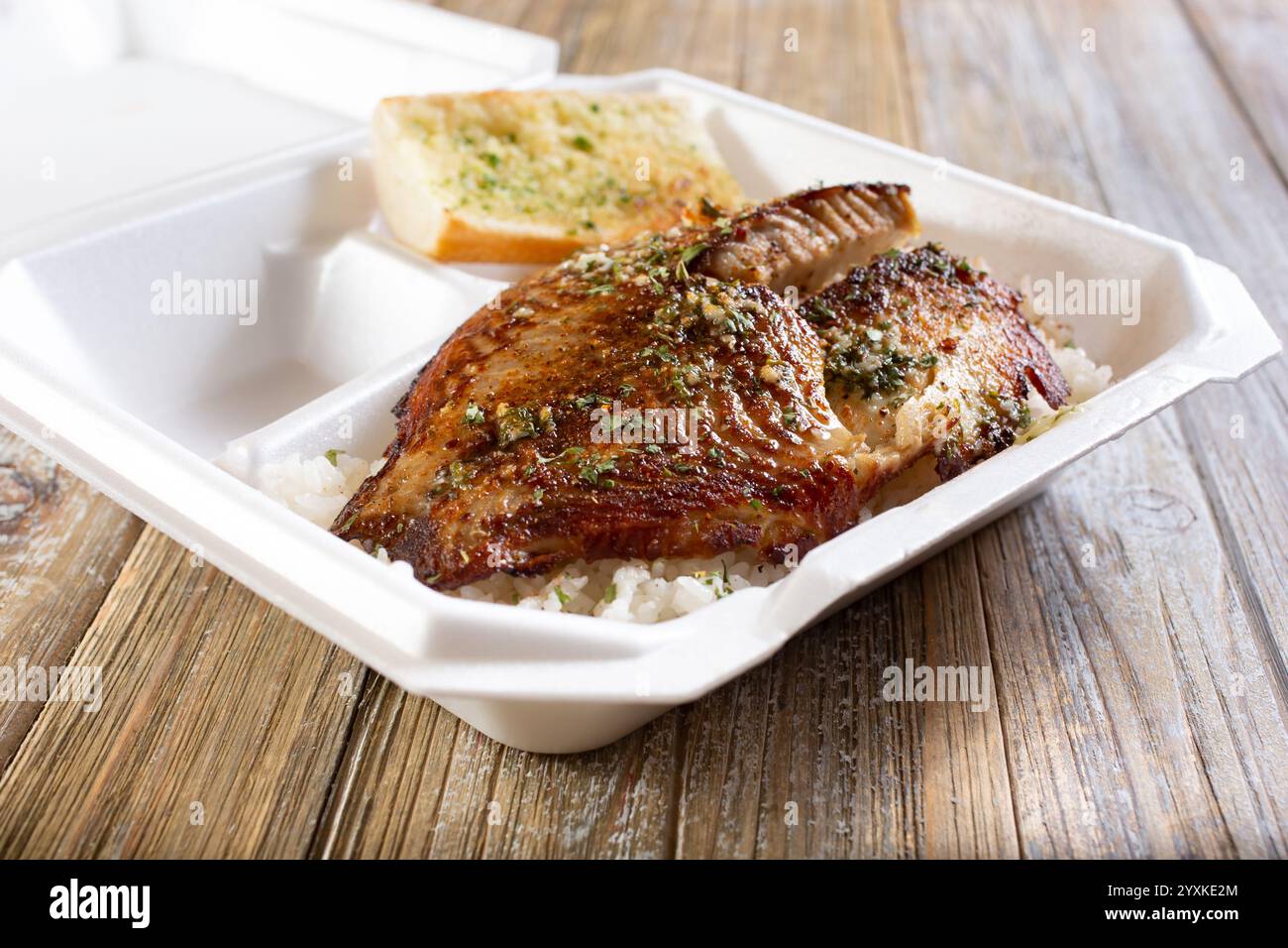 A view of a grilled tilapia over white rice, inside a to-go styrofoam ...