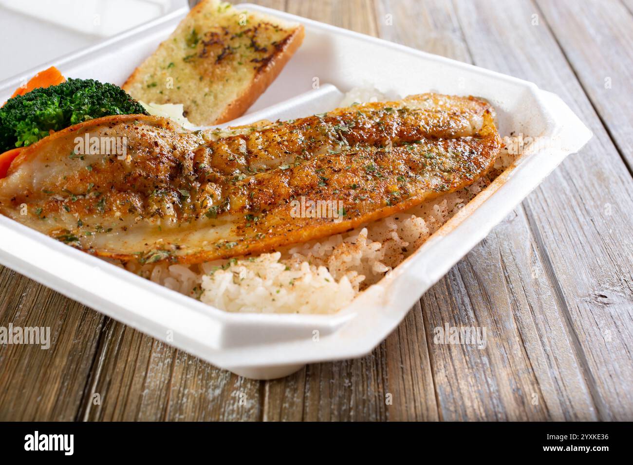 A view of a to-go container featuring a grilled white fish fillet ...