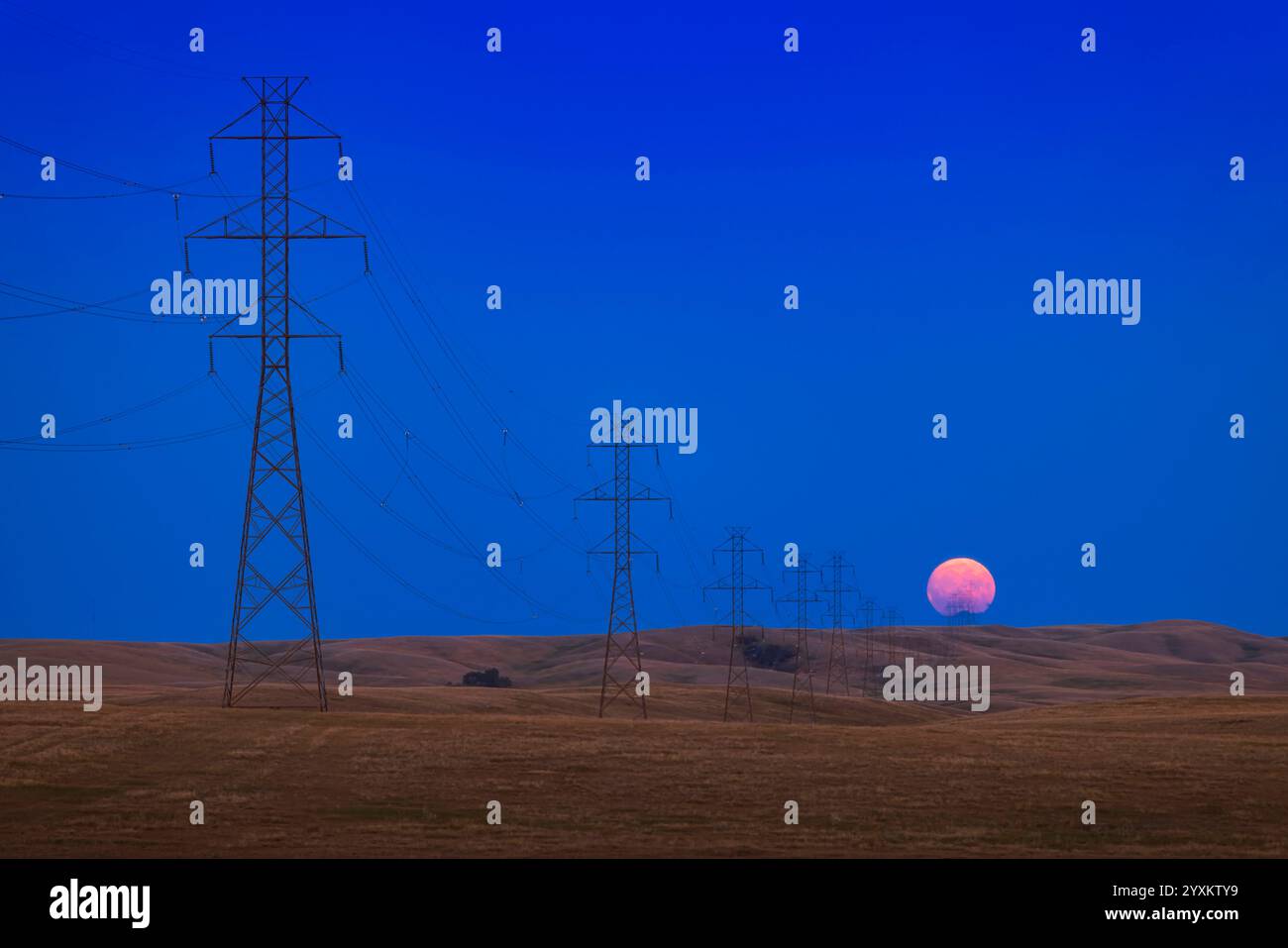 Full Moon rising at the end of a long line of high tension towers in ...
