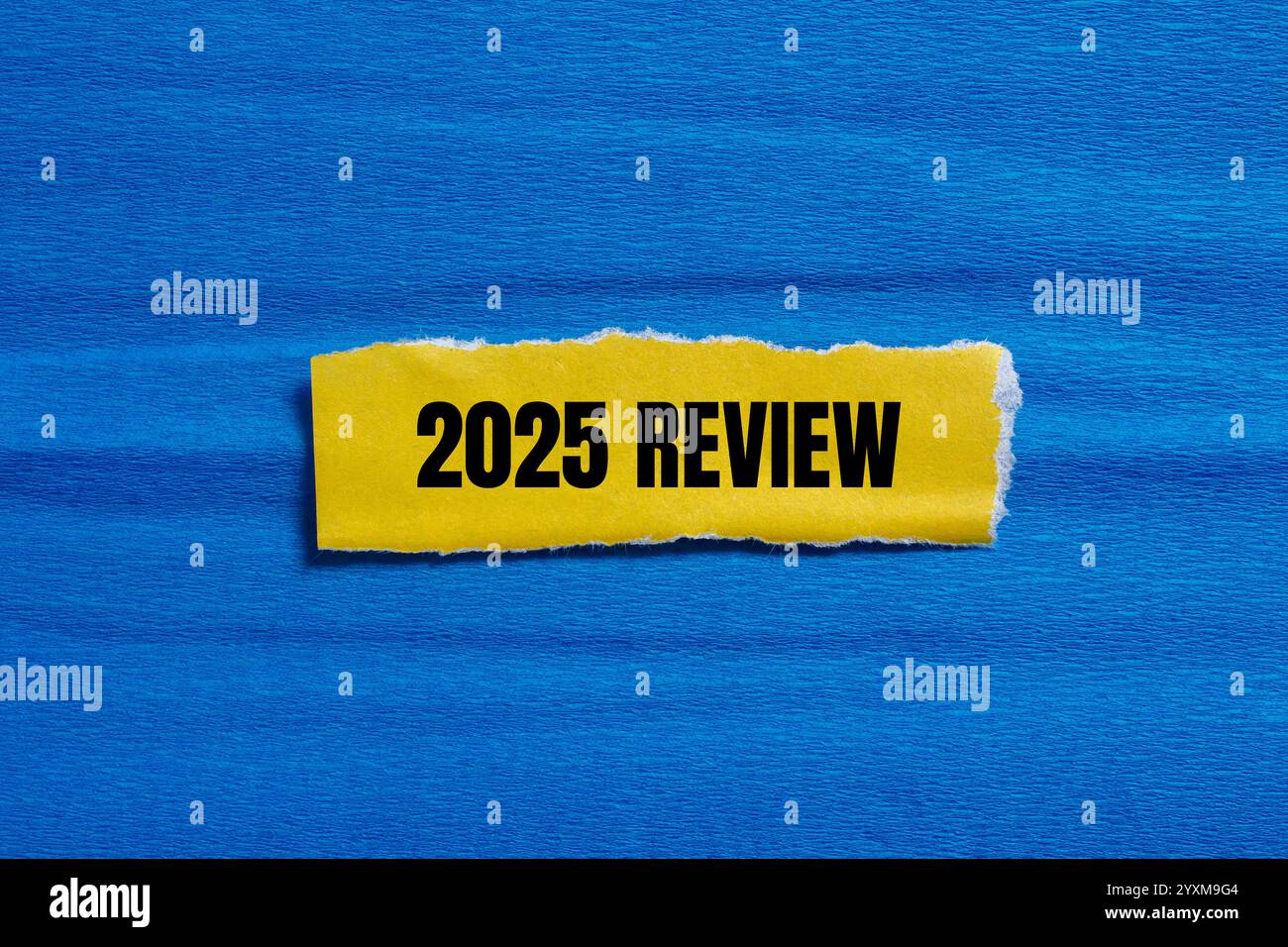 2025 review message written on ripped torn yellow paper piece with blue background. Conceptual ...
