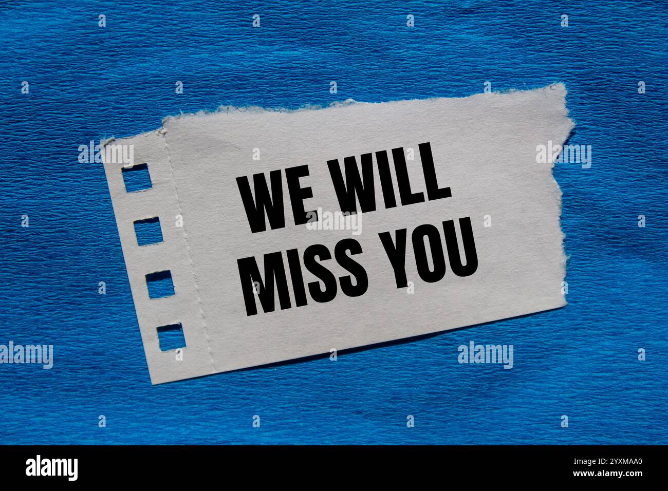 We will miss you message written on ripped torn paper piece with blue background. Conceptual we ...