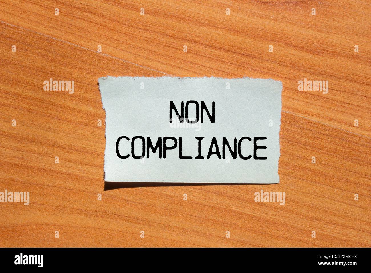 Non compliance message written on ripped torn paper piece with wooden background. Conceptual non ...