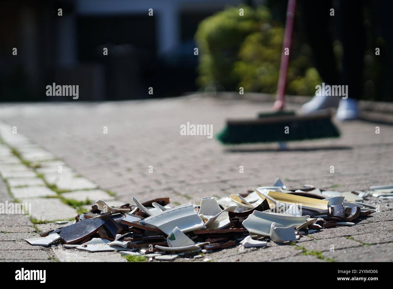A person is sweeping up broken glass on a sidewalk. The scene is messy ...