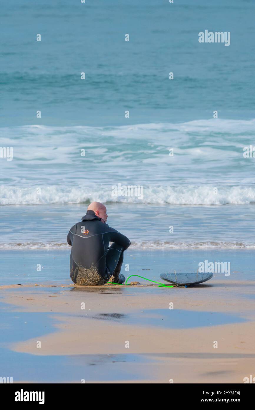A male surfer taking a break and sitting with his surfboard on the ...