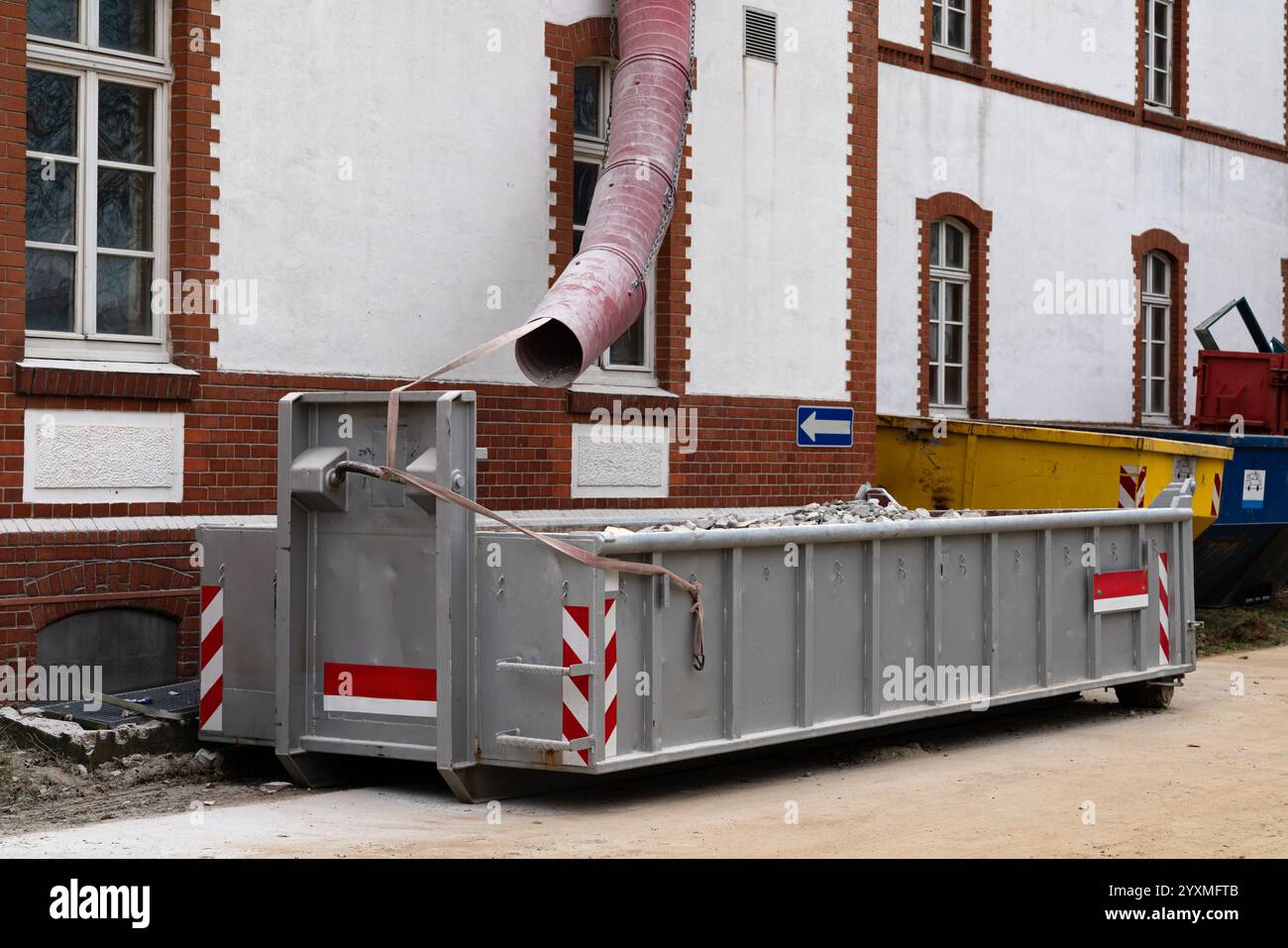 A large waste disposal container sits at a construction site next to a ...