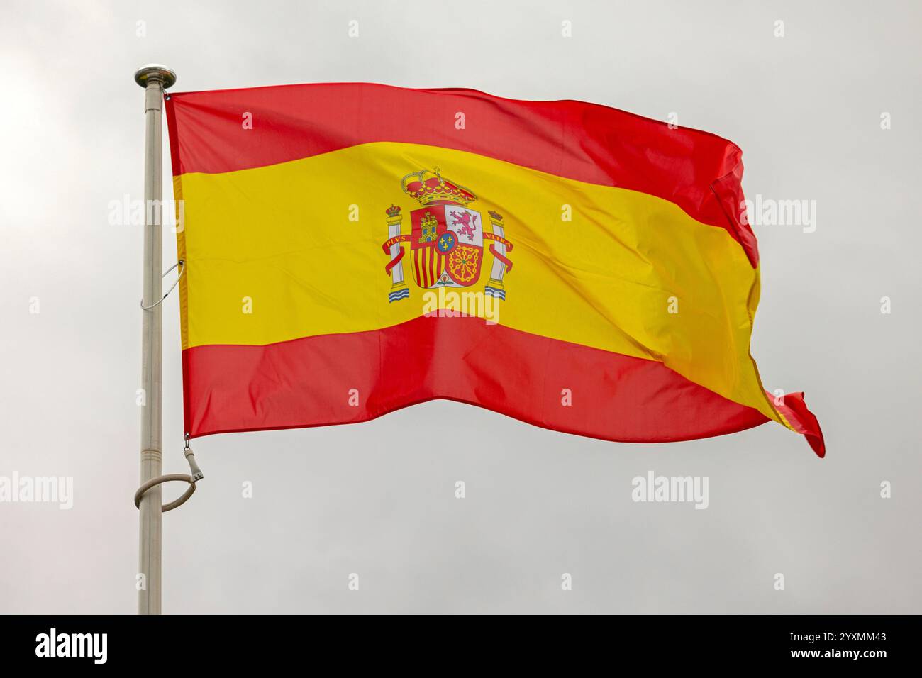official-flag-of-spain-with-coat-of-arms-over-cloudy-sky-stock-photo