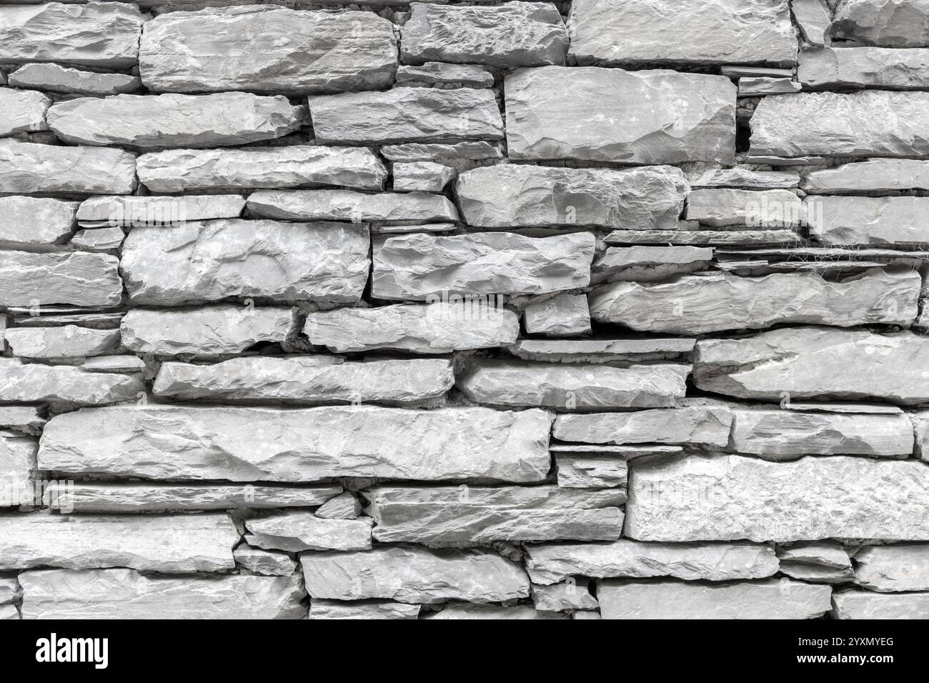 an aged stone wall, with irregularly shaped stones stacked horizontally ...