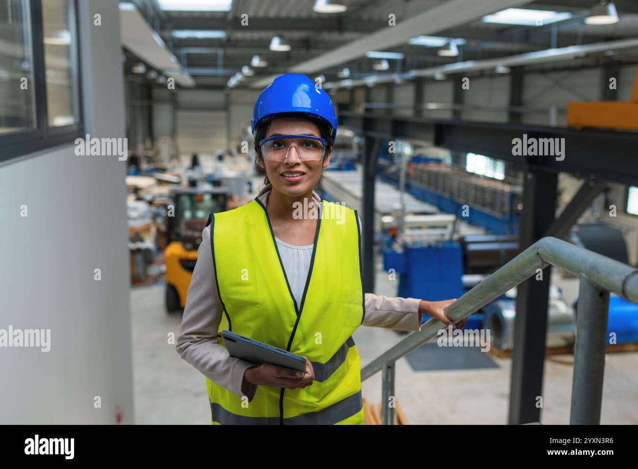 Female industrial plant employee with a blue helmet and yellow vest in ...