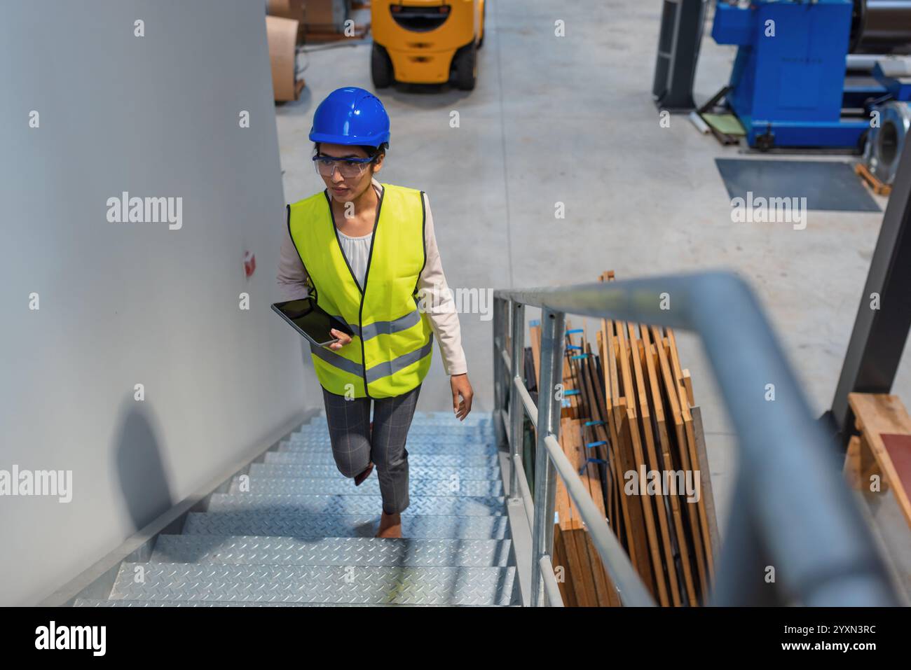 Female industrial plant employee with a blue helmet and yellow vest in ...