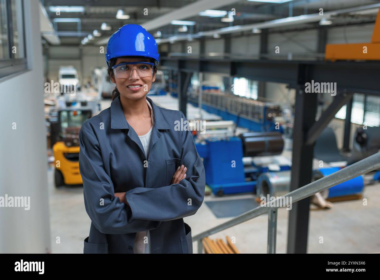 Confident young engineer, an Indian woman, in a blue helmet and gray ...