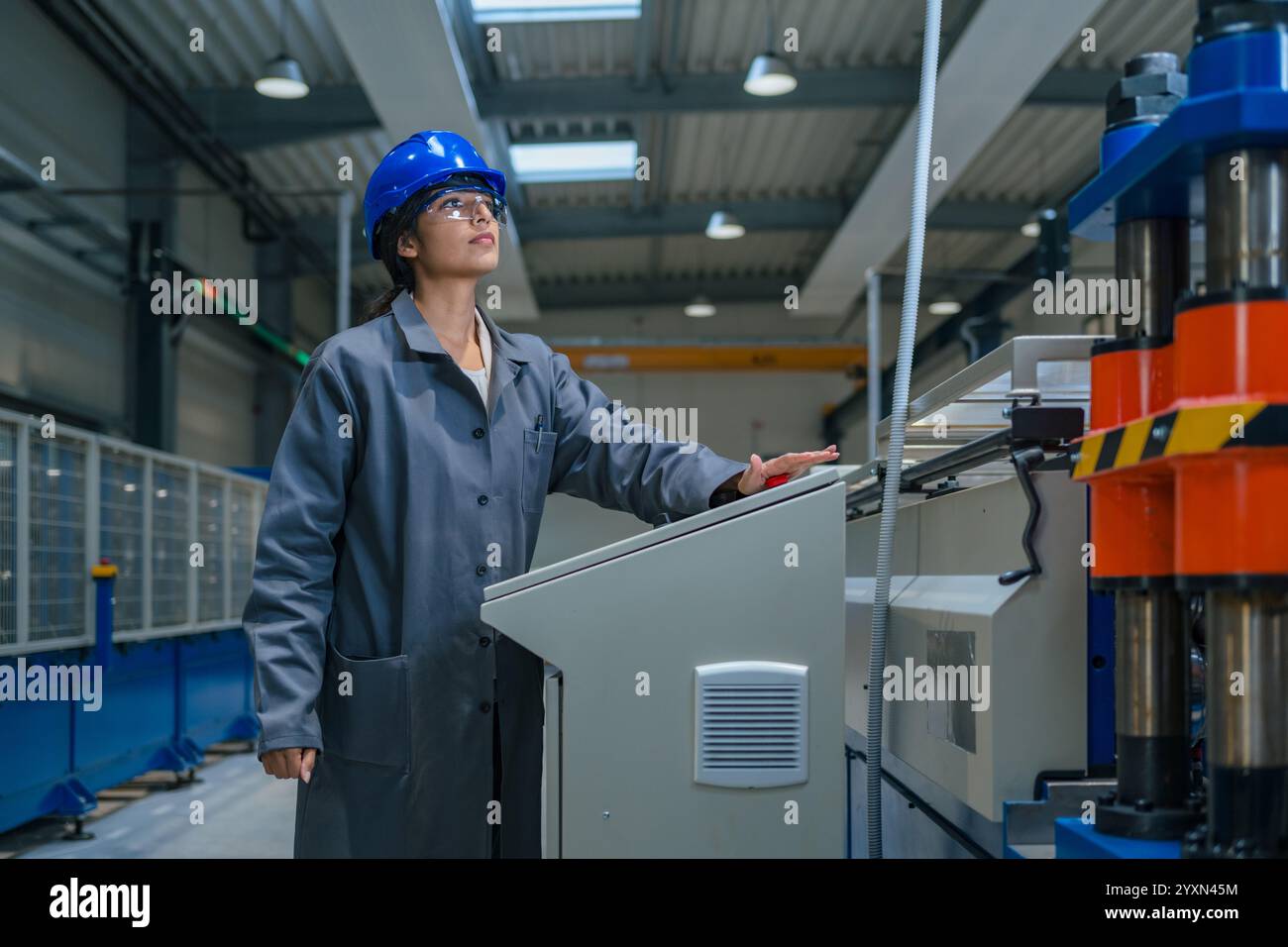 Indian woman engineer with a blue helmet and safety goggles, operating a control panel ...