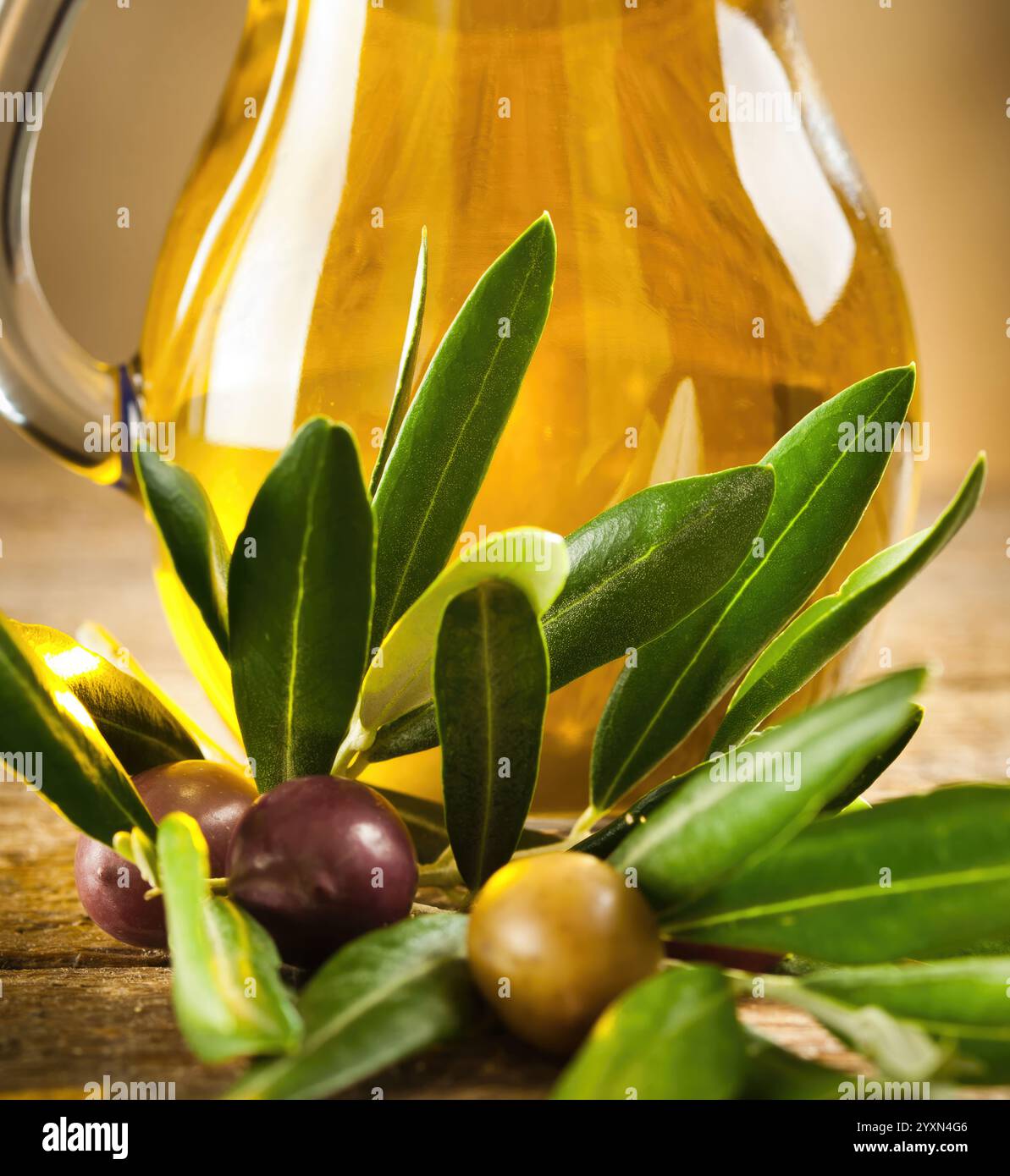 Glass jug filled with golden olive oil, accompanied by fresh olives and ...