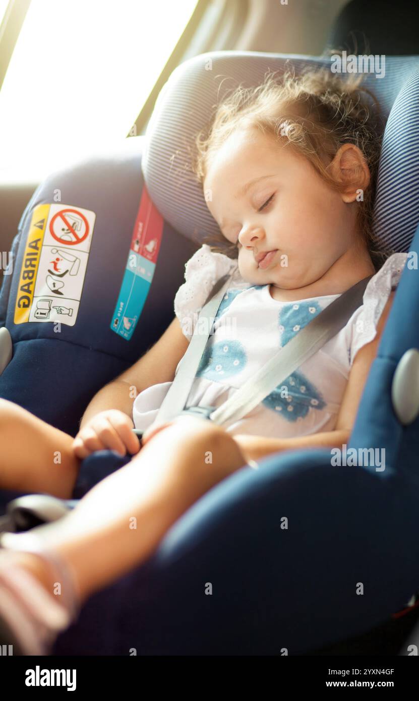 Toddler girl sleeping serenely in a car seat, secured by safety belts ...