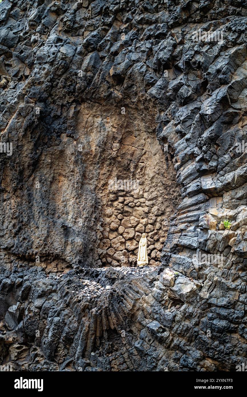 A statue of the Virgin Mary placed within an intricate rocky grotto ...