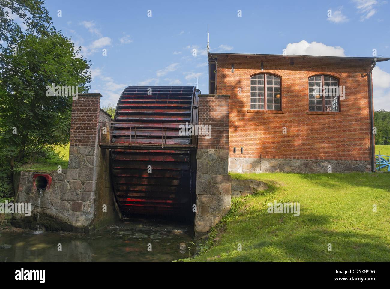 A large waterwheel next to a brick building in a green setting, engine ...