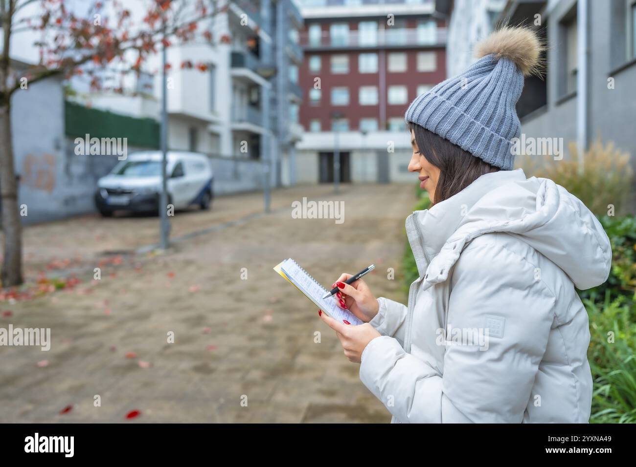 Side view of a caucasian young woman in warm clothes writing notes ...