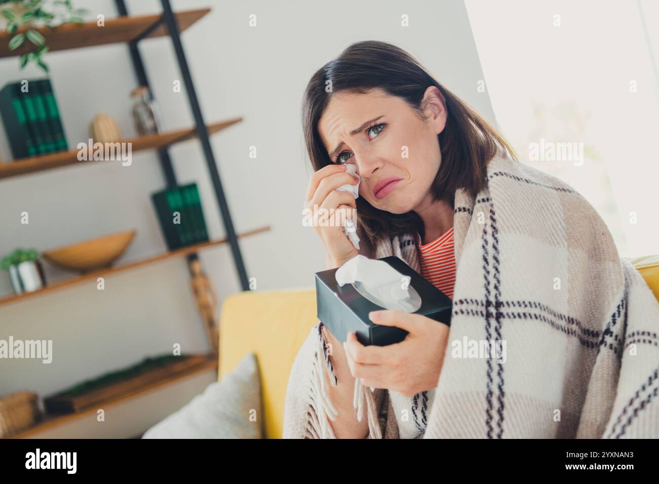 Emotional woman in living room wrapped in blanket, feeling sad, holding ...