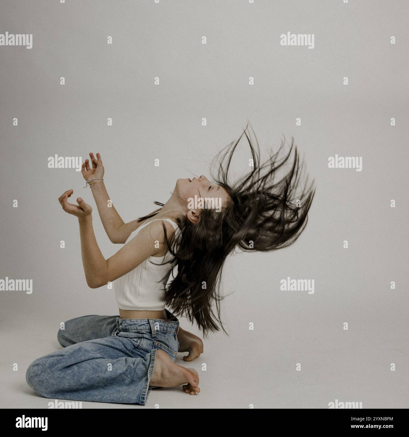 Dark-haired girl, 10, in blue jeans, sits on the floor and throws her ...