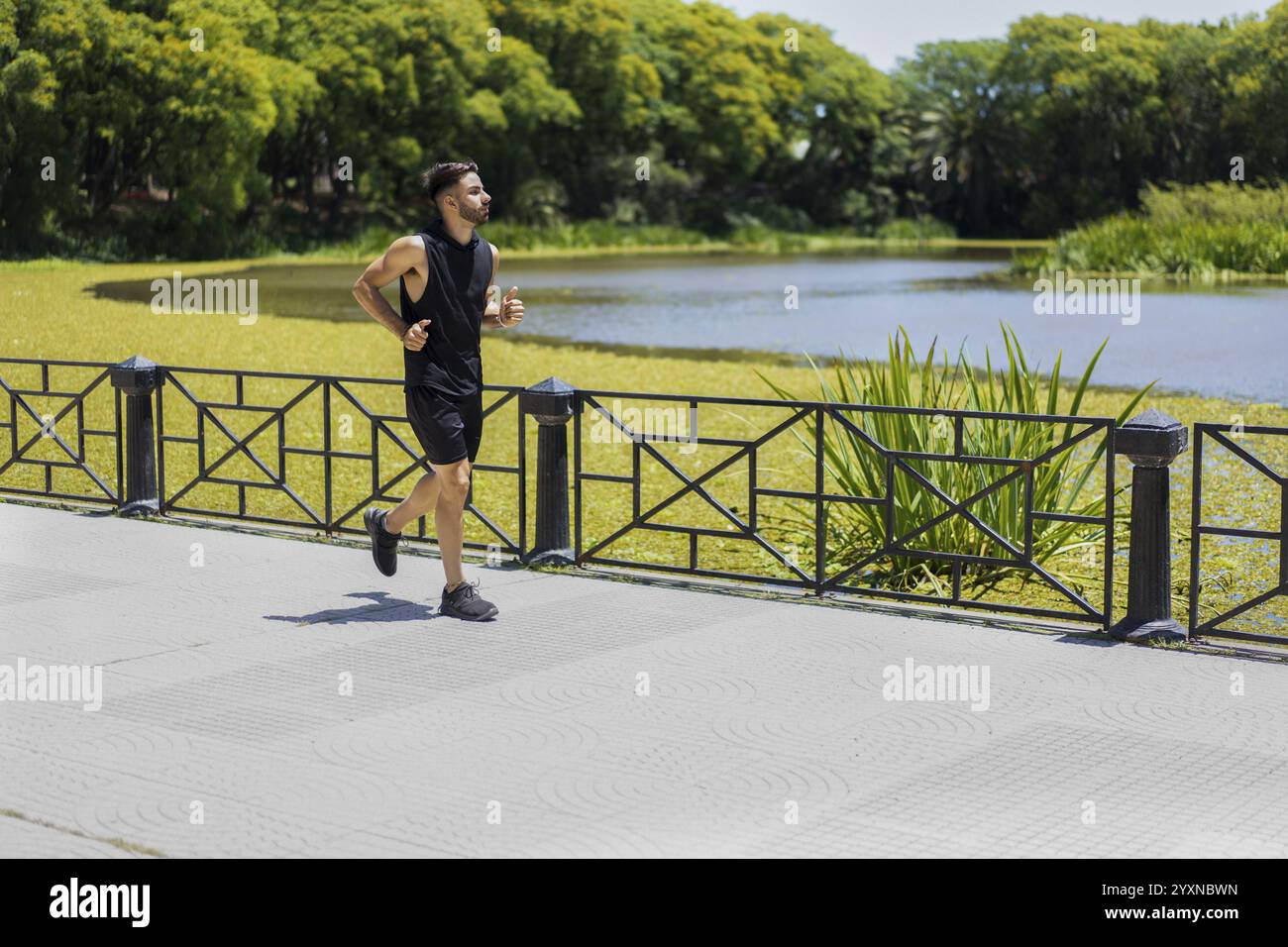 Energized young man running by the lakeside in an urban park setting ...