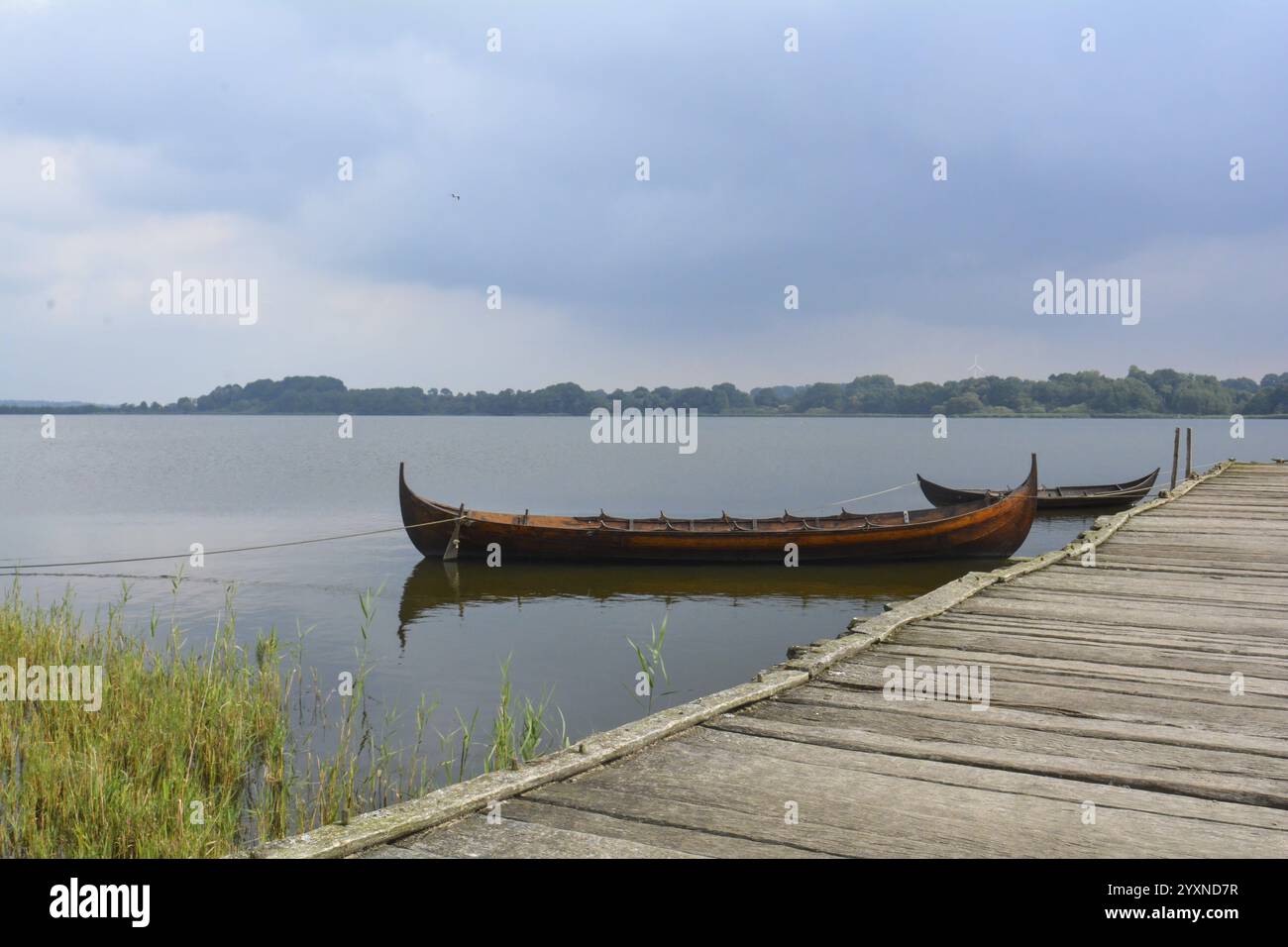Two reconstructed viking boats are tied to a wooden pier on a lake ...