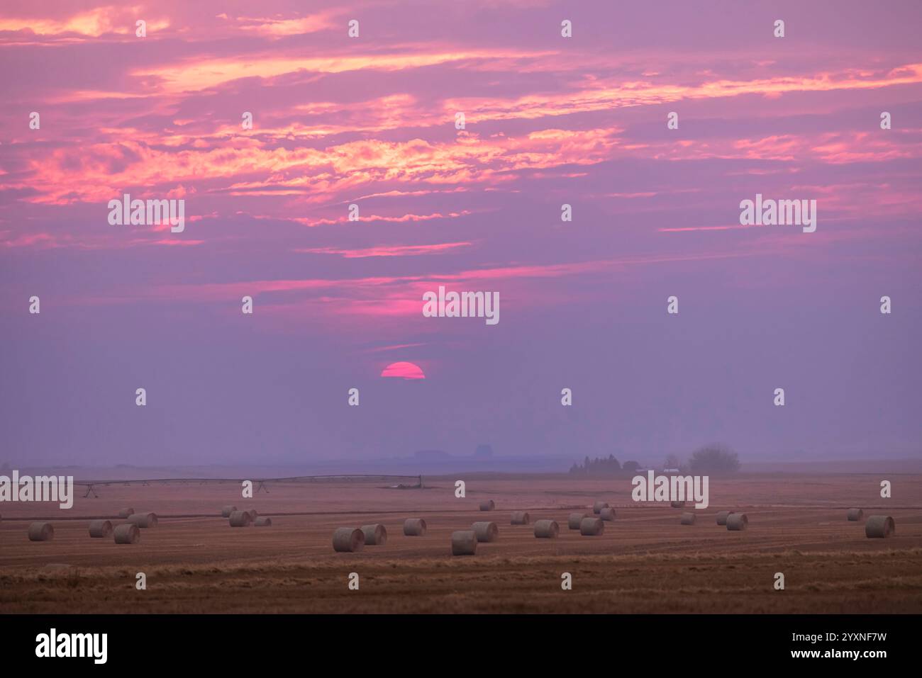 The Sun setting in a smoky and cloudy sky over a harvested grain field ...