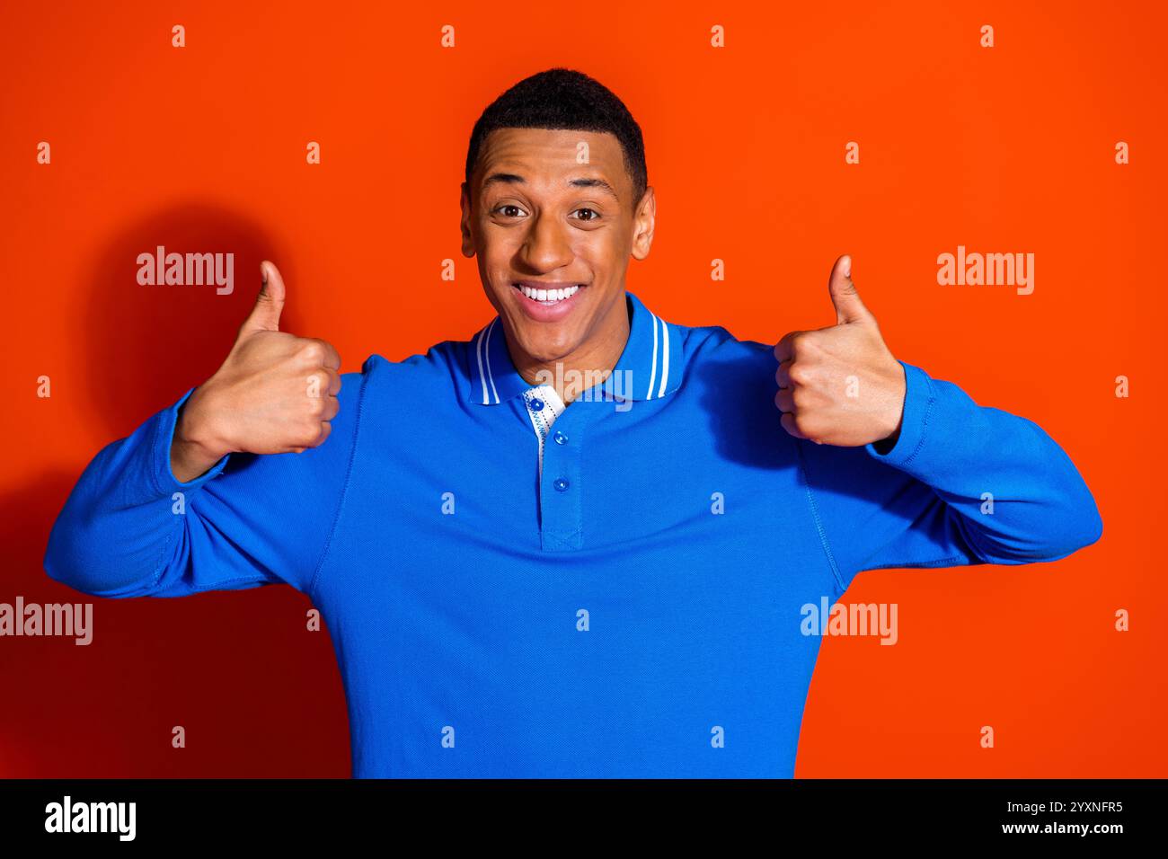 Joyful young man giving a double thumbs up with an orange background ...
