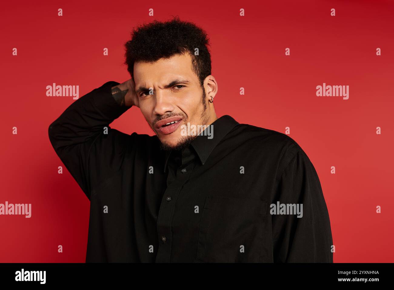 A handsome young man stands with a hand on his neck, displaying a ...