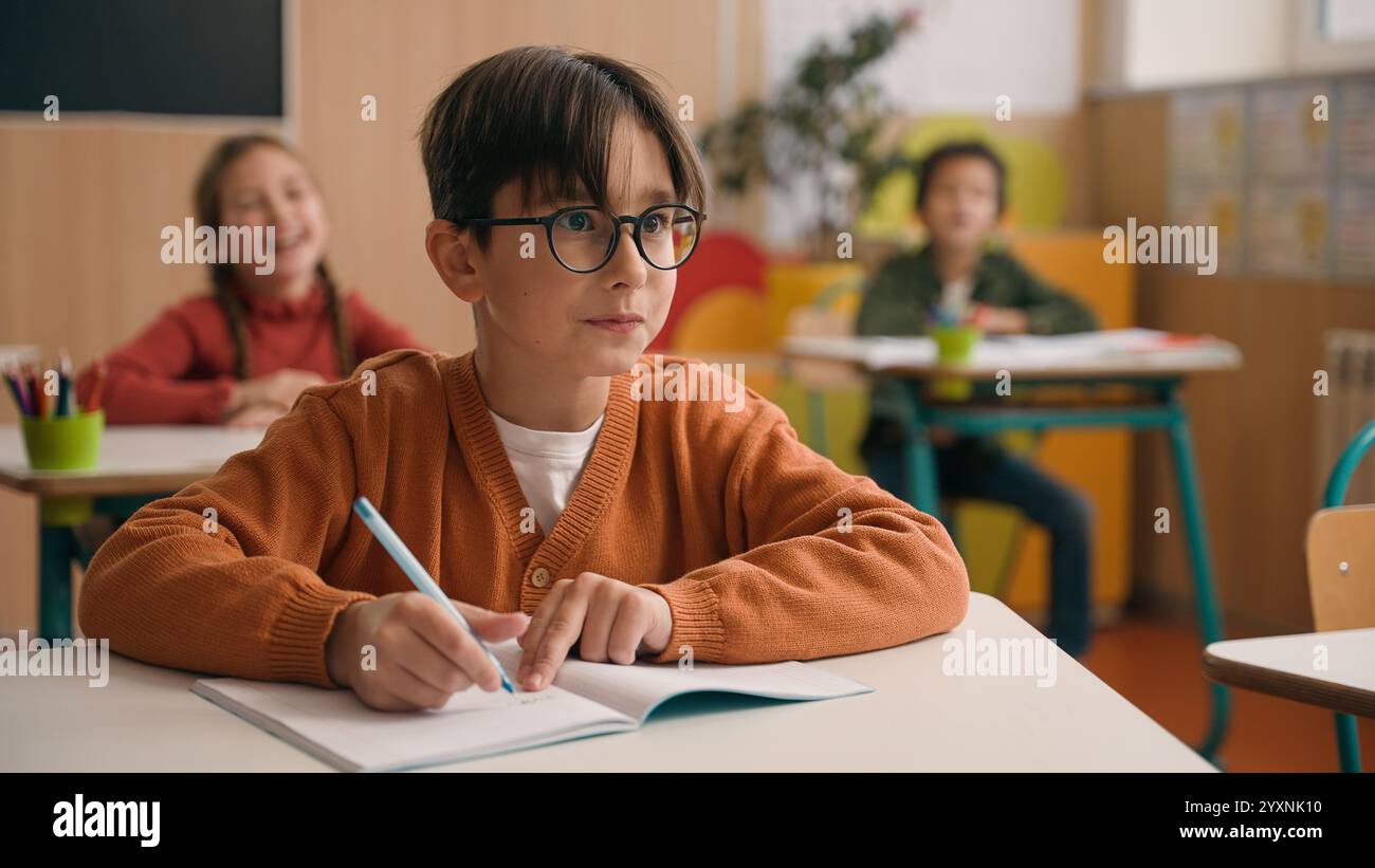 Caucasian little boy kid schoolboy nerd in glasses write task class ...