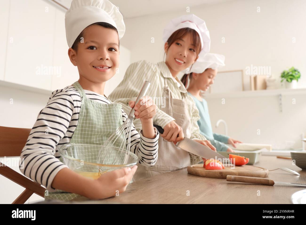 Female Asian chef with her little children cooking apple pie in kitchen ...