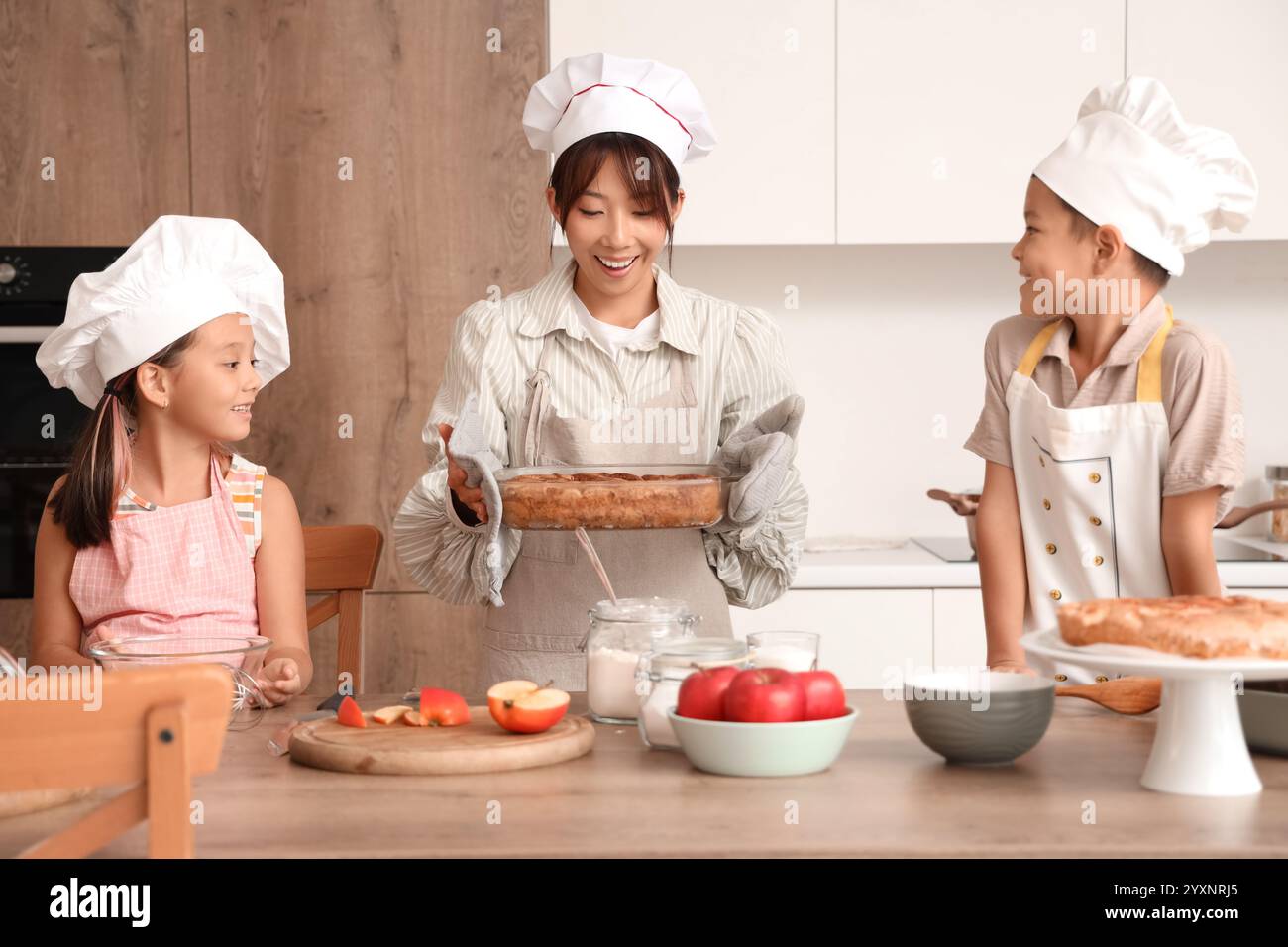 Female Asian chef with tasty pie and her little children cooking in ...
