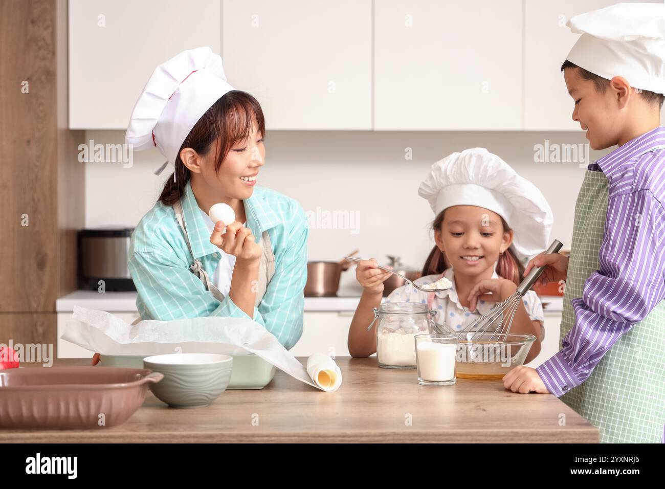 Female Asian chef with her little children making dough in kitchen ...