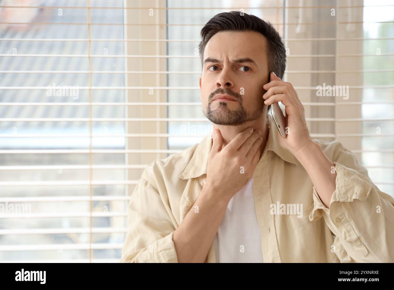 Handsome man with thyroid gland problem talking by mobile phone at home ...