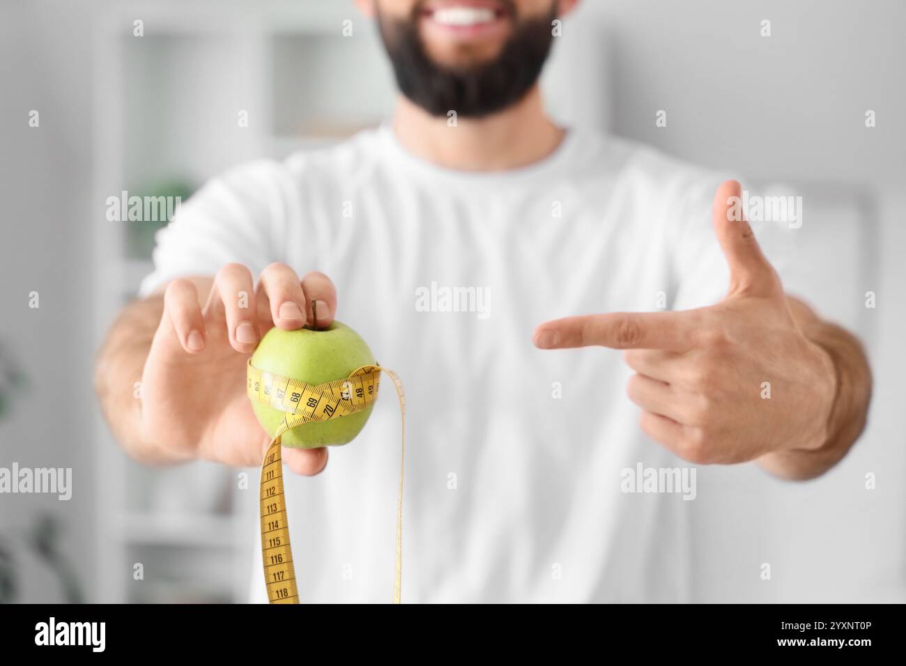 Sporty young man pointing at apple with measuring tape at home, closeup ...