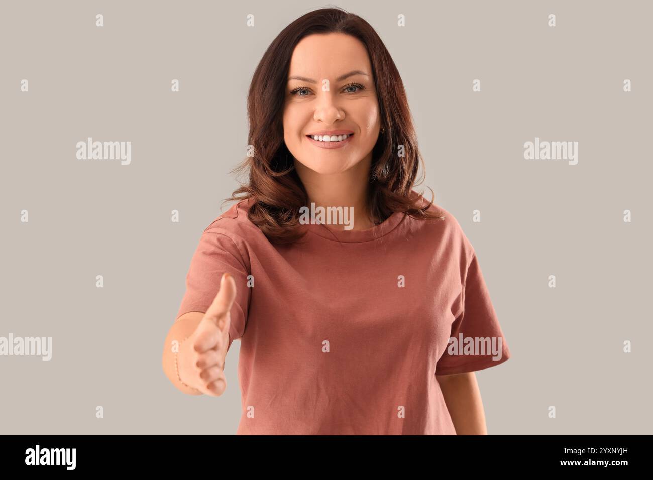 Beautiful happy mature woman extending hand for handshake on grey ...