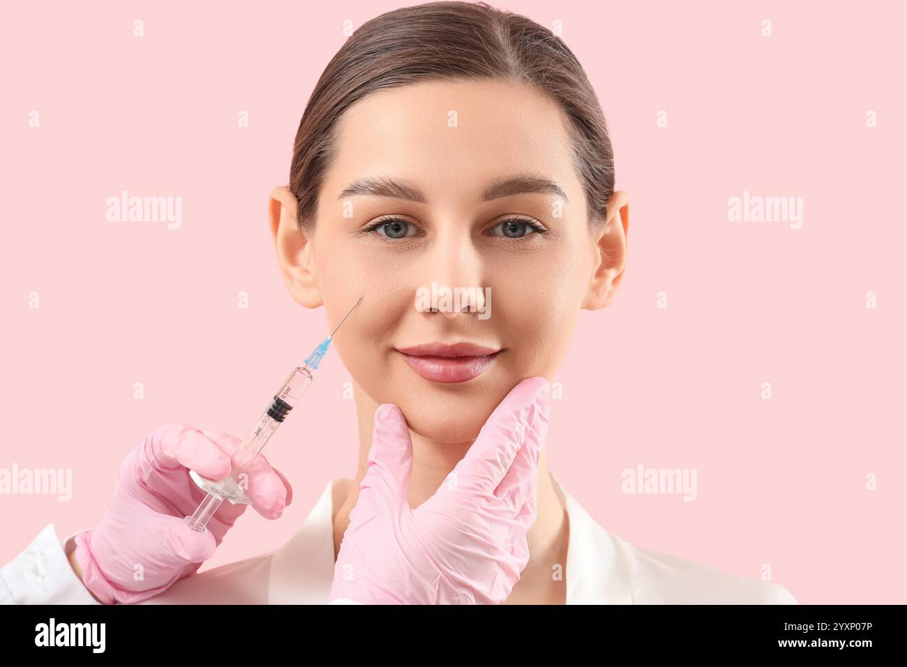 Young girl receiving filler injection in face against pink background ...