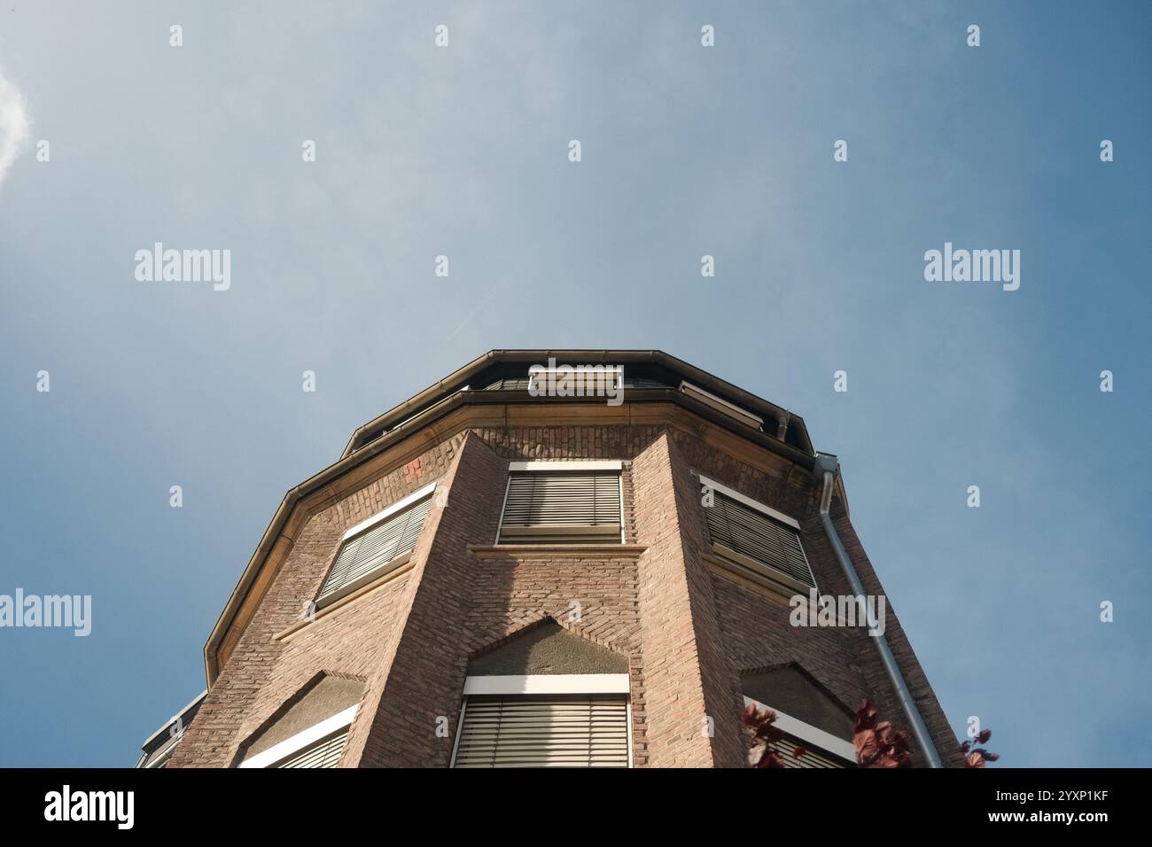A tall brick building with a slanted roof and a window on the top. The ...