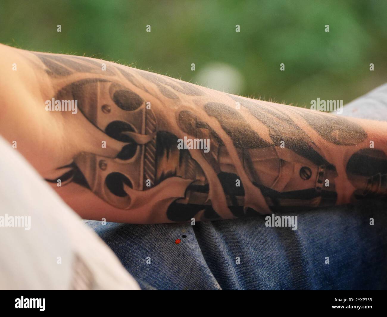 A man's arm has a tattoo of a gun and a machine gun. The tattoo is ...