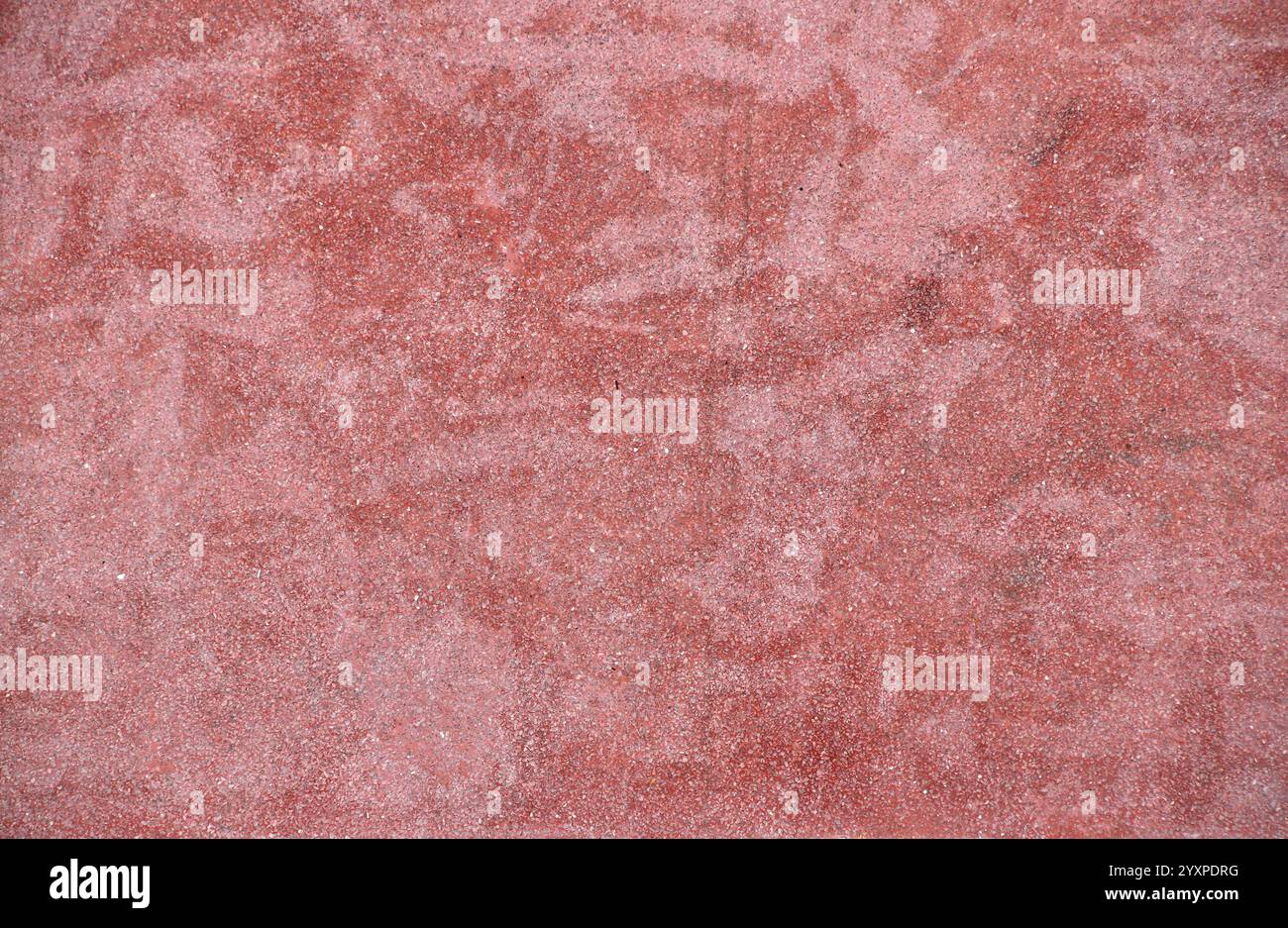 Red concrete stone surface displays rough texture and color variation, creating a natural and ...