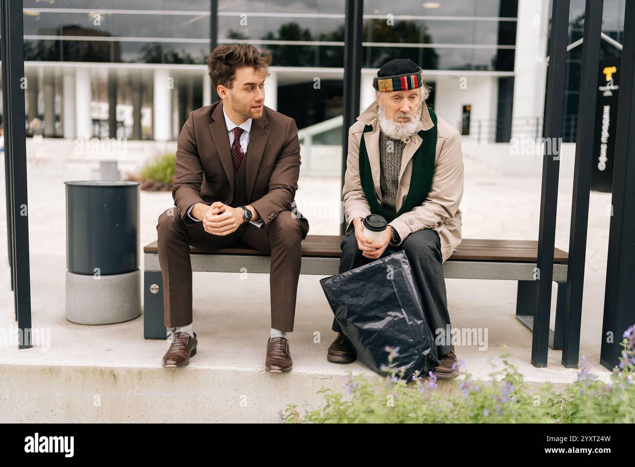 Front view of chatting young businessman and old homeless man sitting ...
