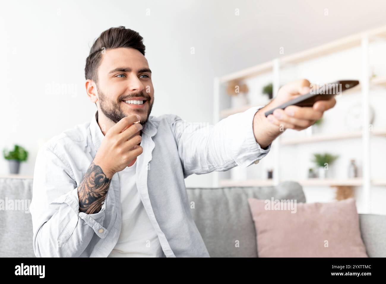 Cheerful millennial guy watching TV and eating popcorn, switching ...