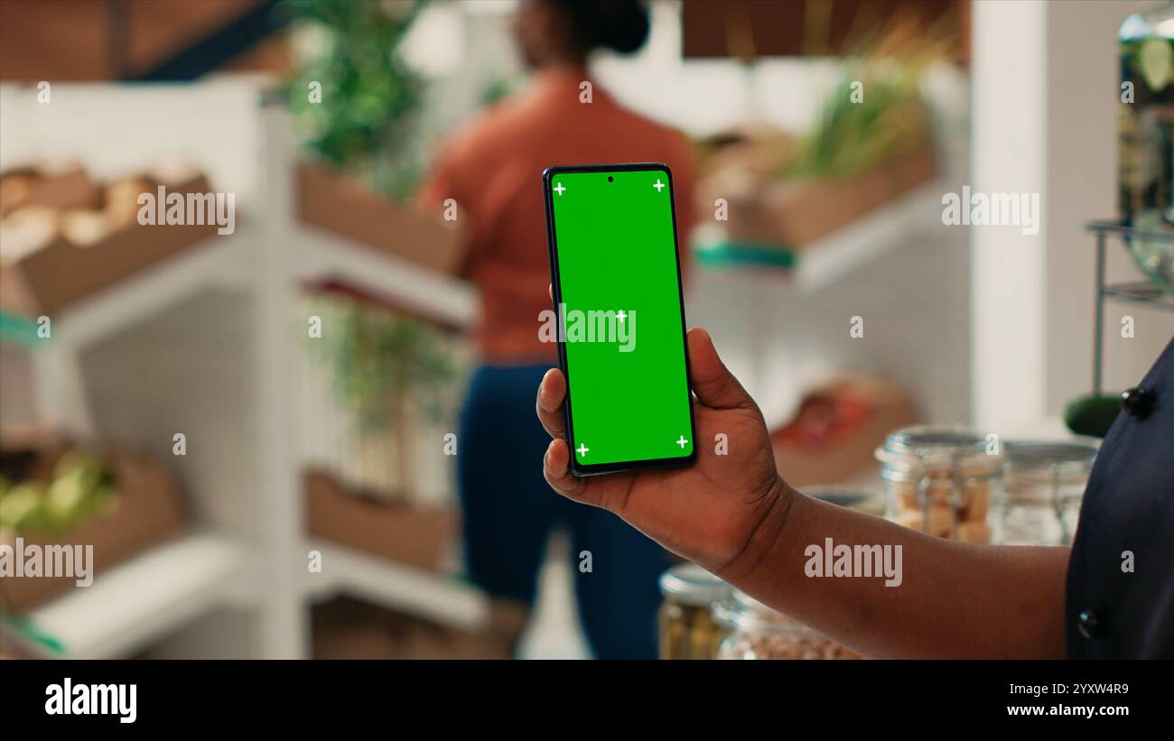 Vendor showing phone with greenscreen layout at supermarket, holding ...