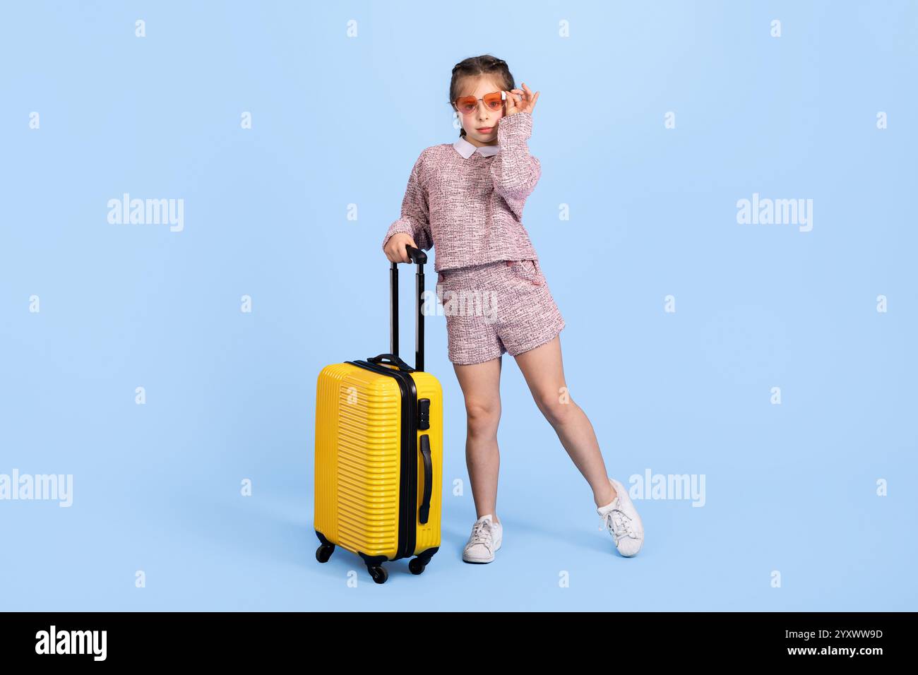 Happy girl in stylish outfit poses with yellow suitcase against blue ...