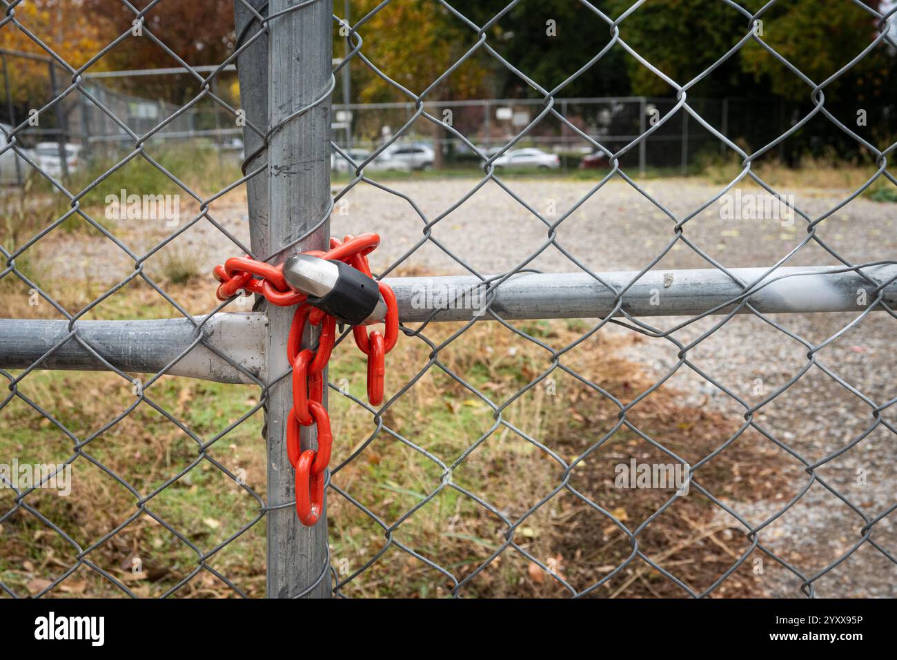 A padlock and red chain on a chain-linked fence around an empty lot in ...