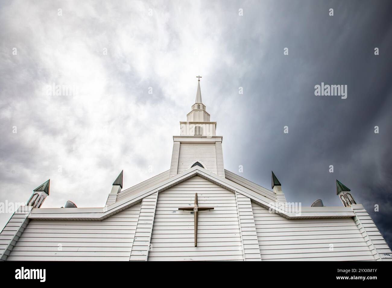 Church steeple with a cross on top rises against a dramatic, cloudy sky ...