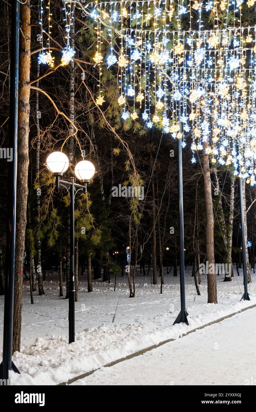 Snow-covered park path is illuminated by warm streetlights, snowflake ...