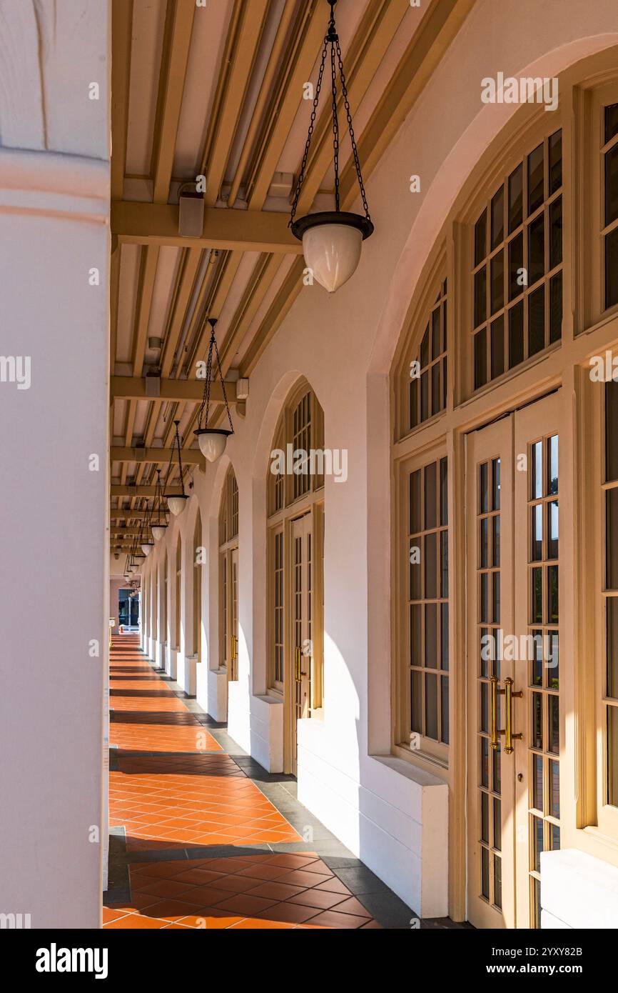 Sunlit corridor with arches and hanging lights in historic Raffles ...